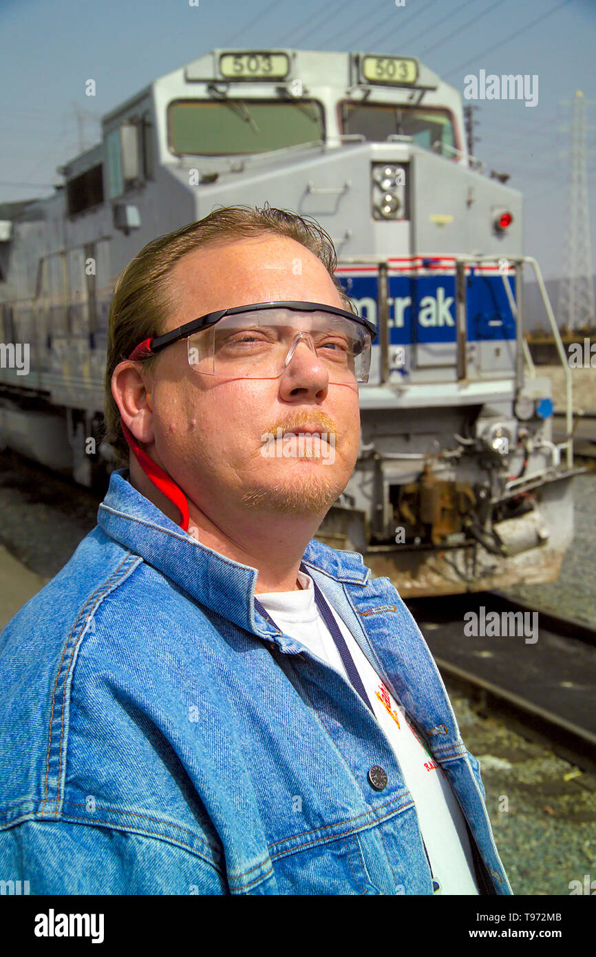Wearing safety glasses, a train engineer poses with his locomotive in a ...