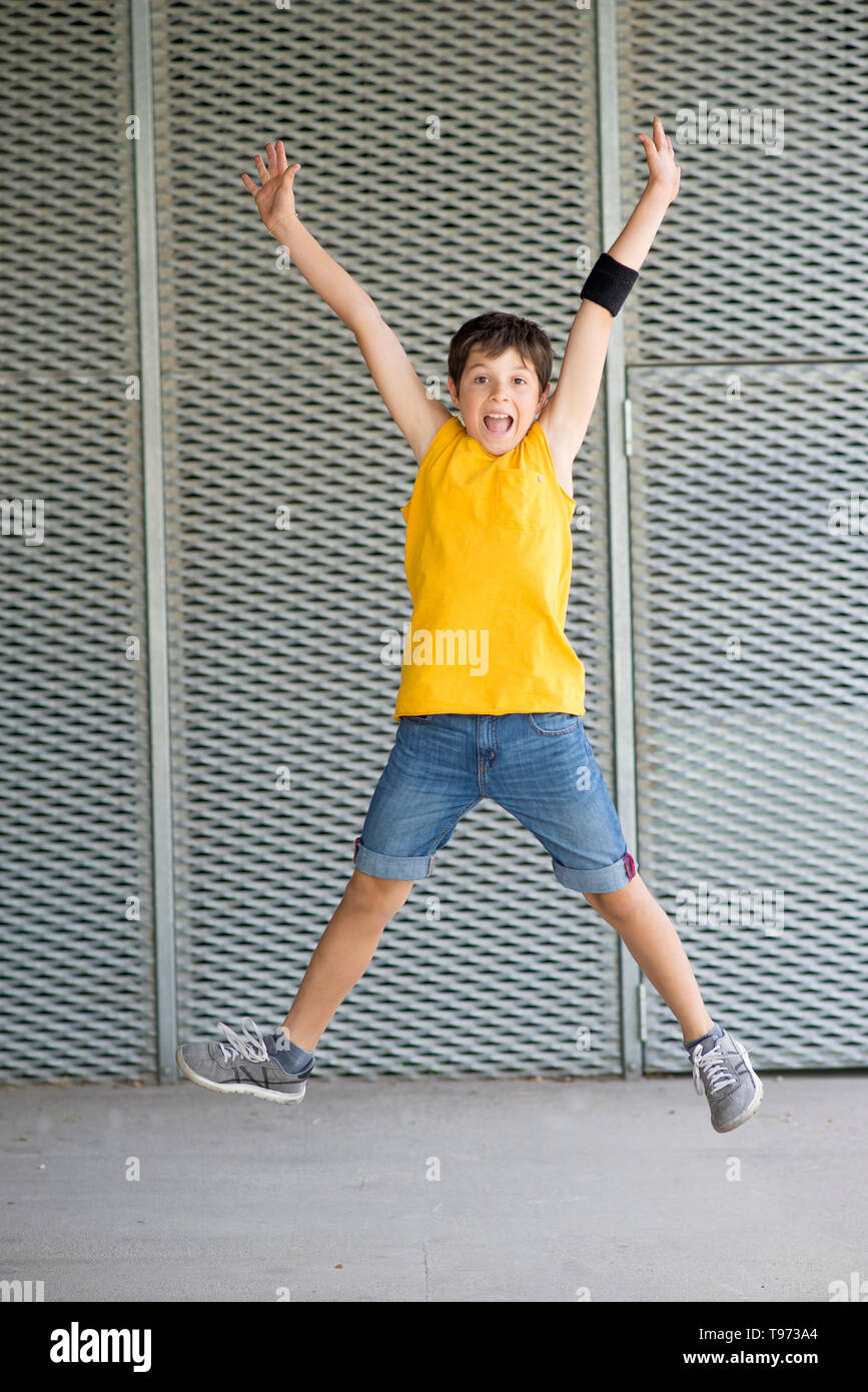 Front view of smiling cheerful boy jumping while arms raised outdoors ...