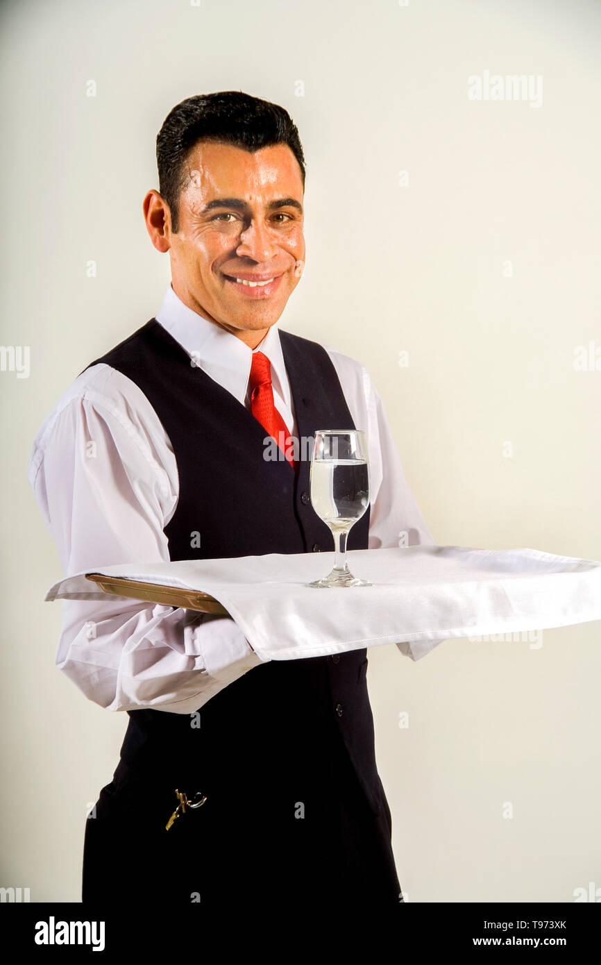 A uniformed Hispanic passenger train waiter poses with a glass of water ...