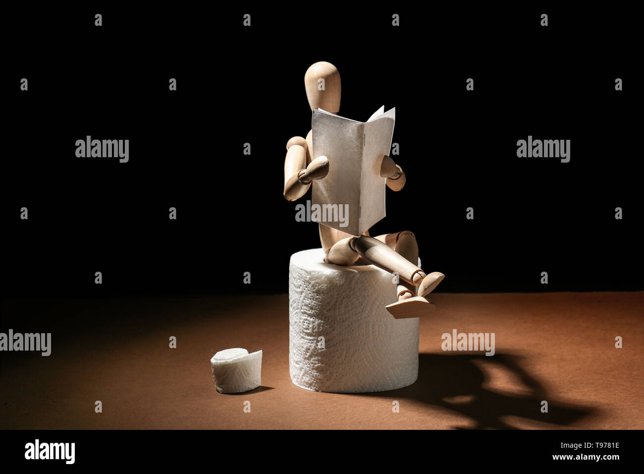 Small wooden mannequin reading newspaper while sitting on toilet paper ...