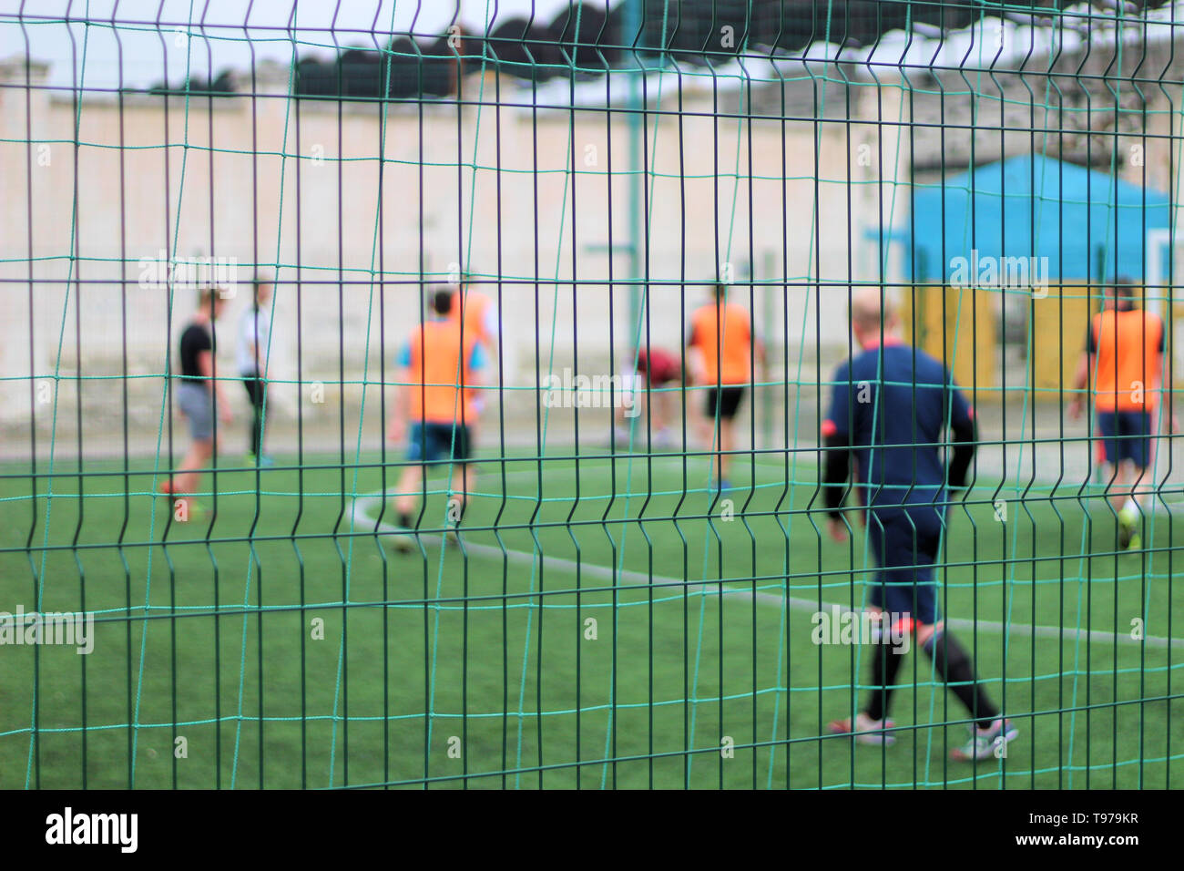 Focused image of sectional green fence. Soccer players with a ball ...