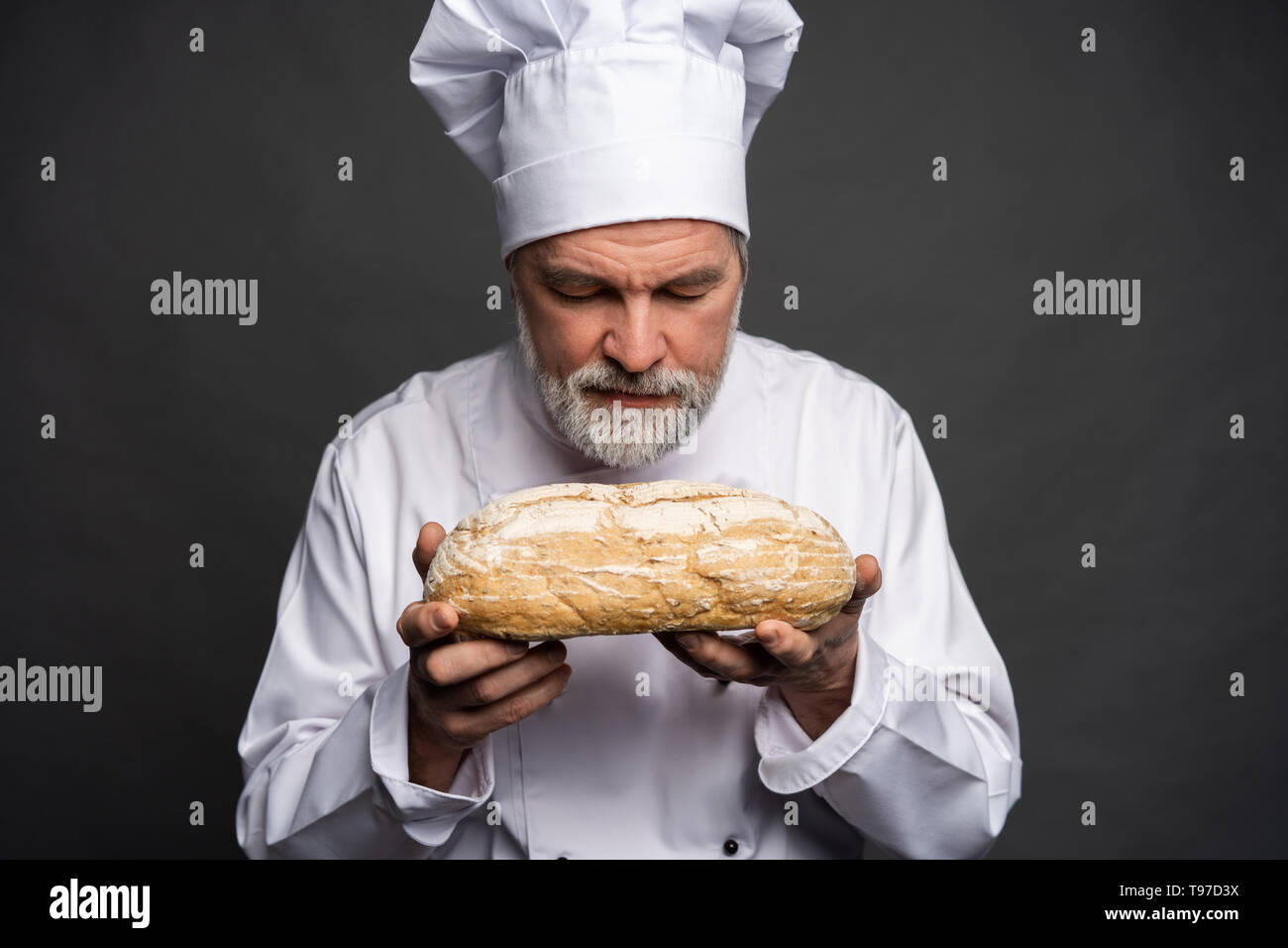 Portrait of a male chef cook smelling fresh bread against black ...