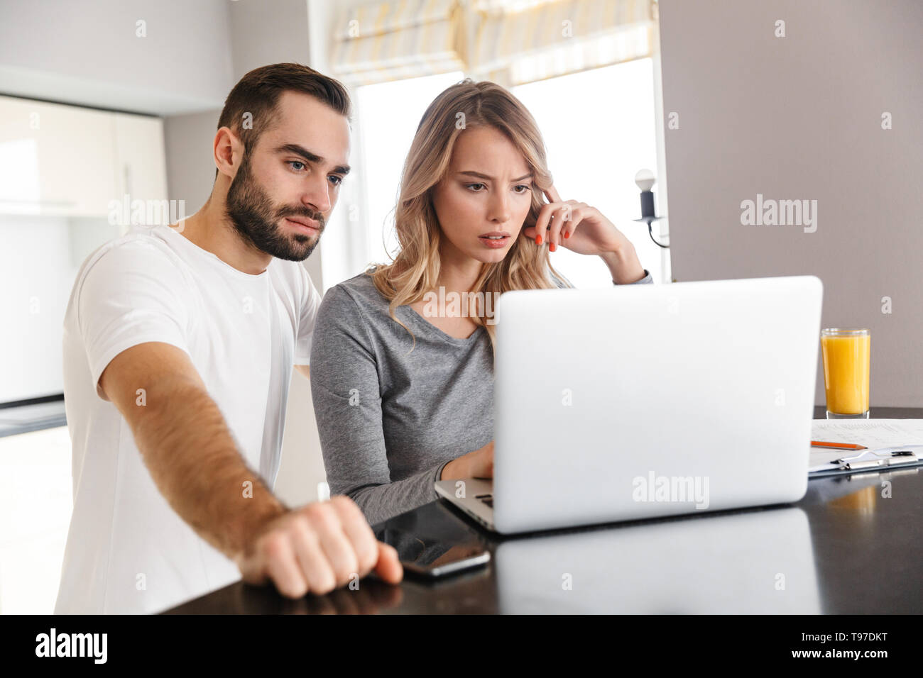 Image of serious loving couple sitting at the kitchen using laptop ...