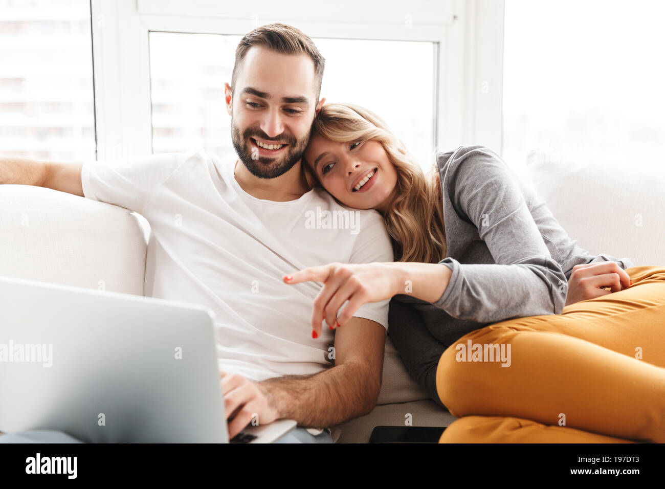 Image of amazing loving couple sitting indoors at home using laptop ...