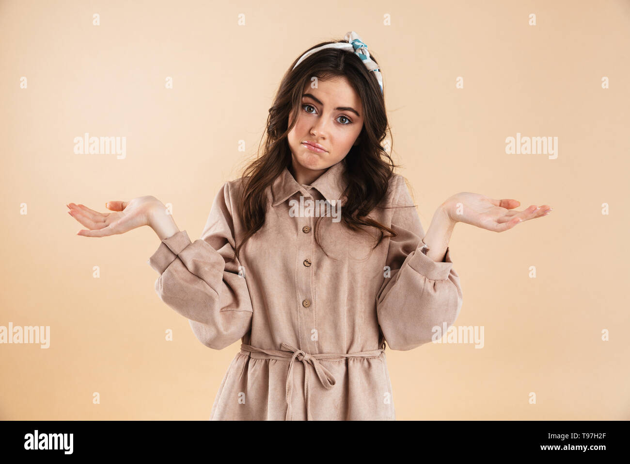 Image of a beautiful confused young woman posing isolated over beige ...