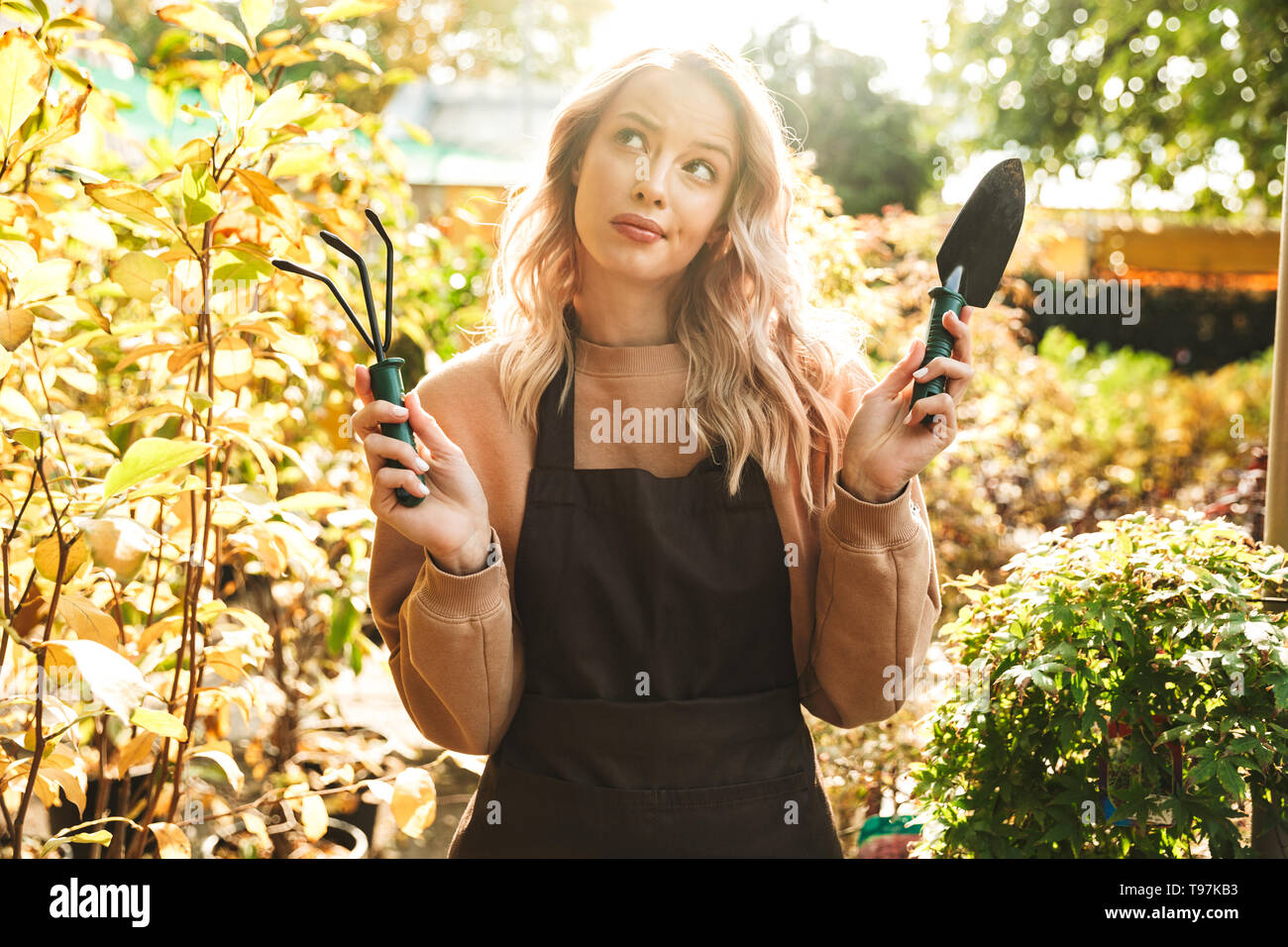 Image of a thinking young woman gardener at the workspace over plants ...