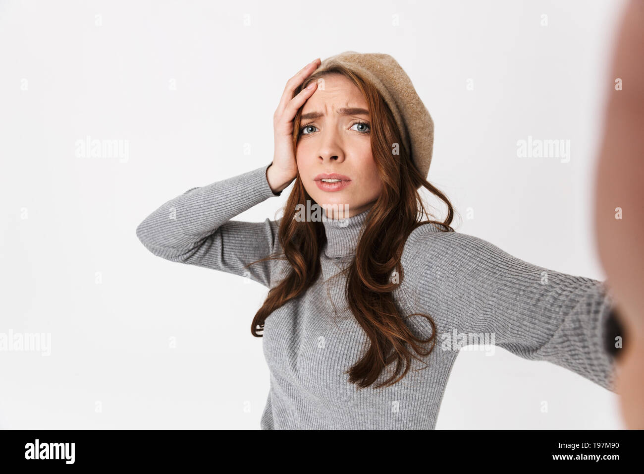 Portrait of serious woman 30s wearing hat frowning while taking selfie ...