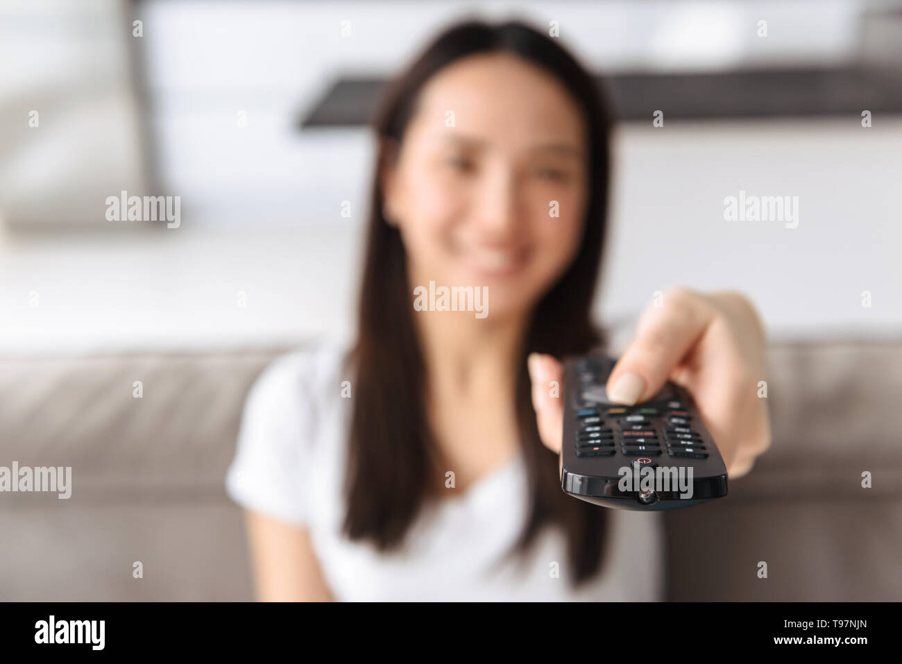 Close up of a smiling asian woman holding TV remote control while ...