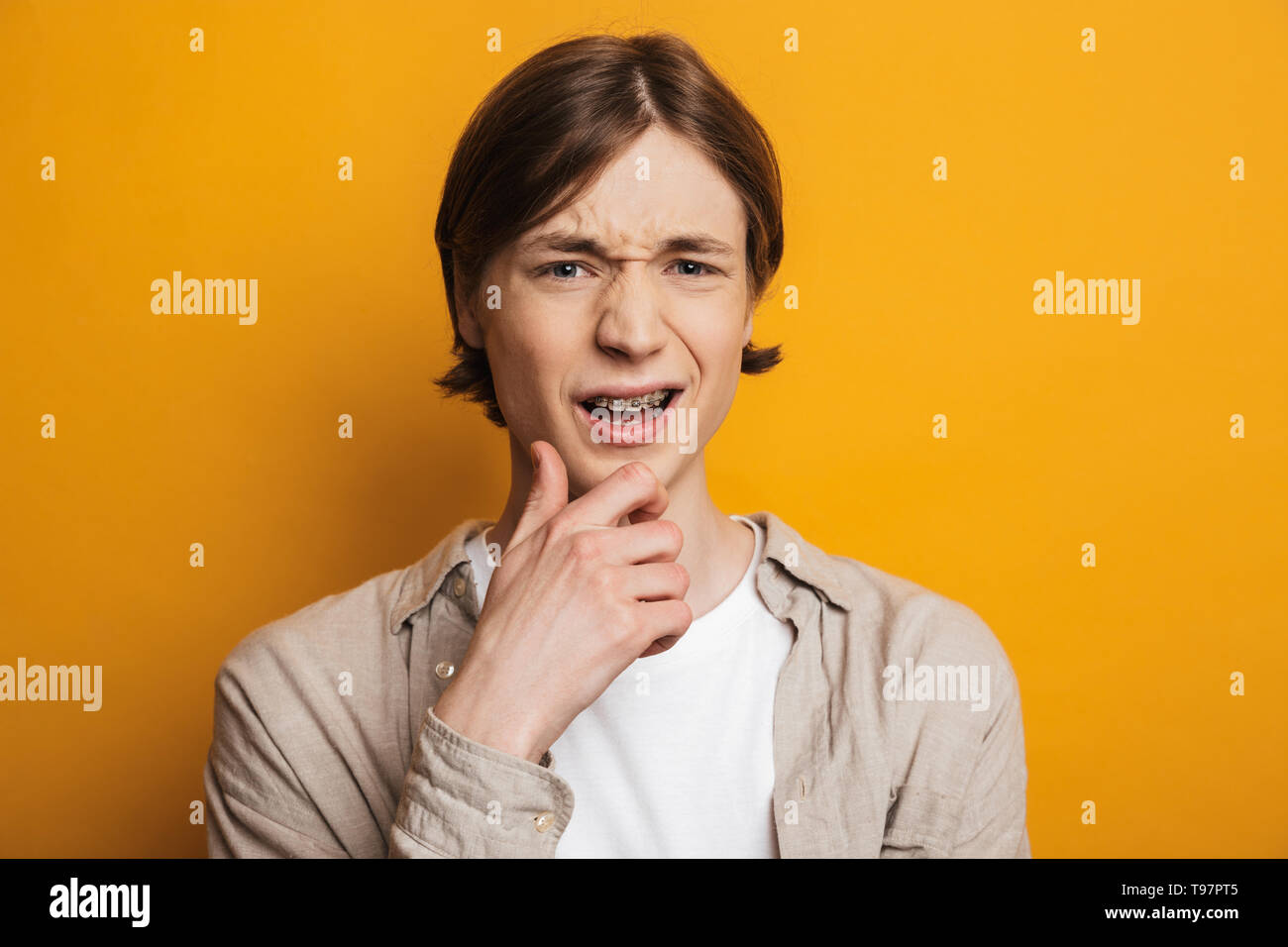 Close up of a confused teenage boy standing isolated over yellow ...