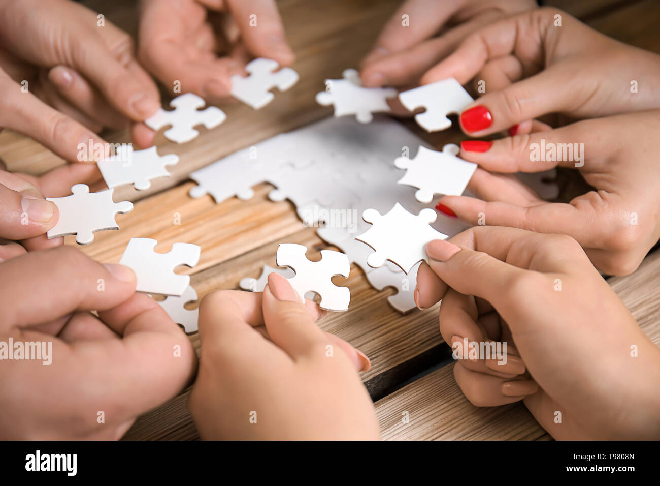 Group of people doing puzzle on table Stock Photo - Alamy