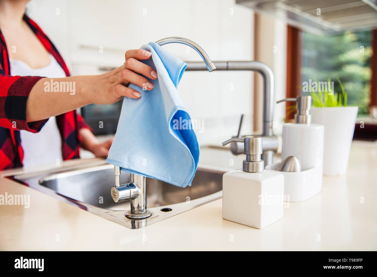 Woman is wiping the sink with blue cloth in the kitchen Stock Photo - Alamy