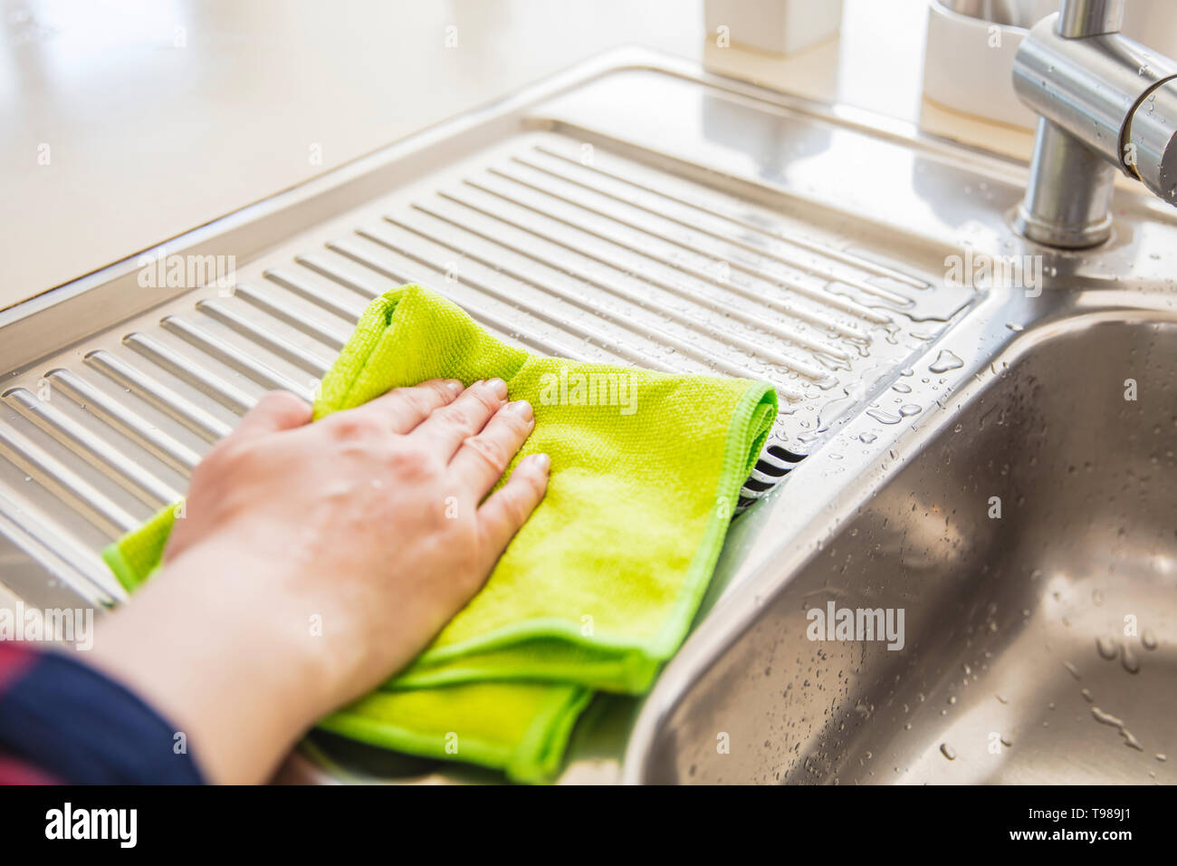 Woman is wiping the water from the drainer in the kitchen with green ...