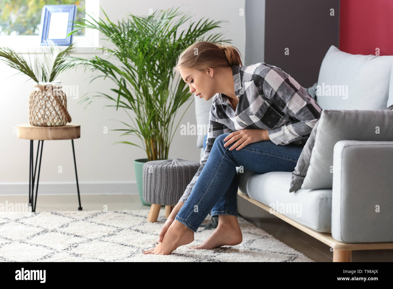 Young woman suffering from leg pain at home Stock Photo - Alamy