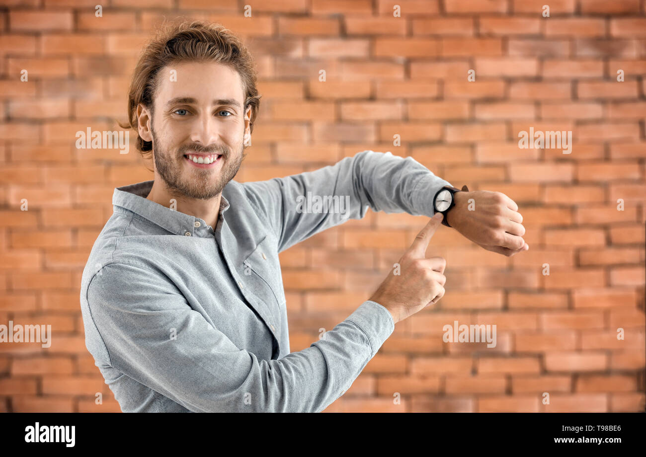 Young man pointing at his watch on brick background Stock Photo - Alamy