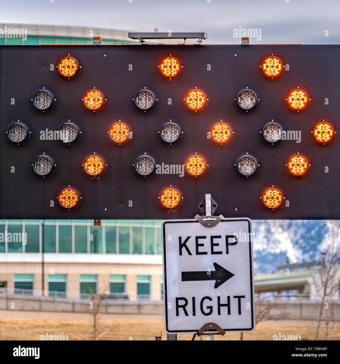 Square Close up of an arrow board and Keep Right sign against a modern ...
