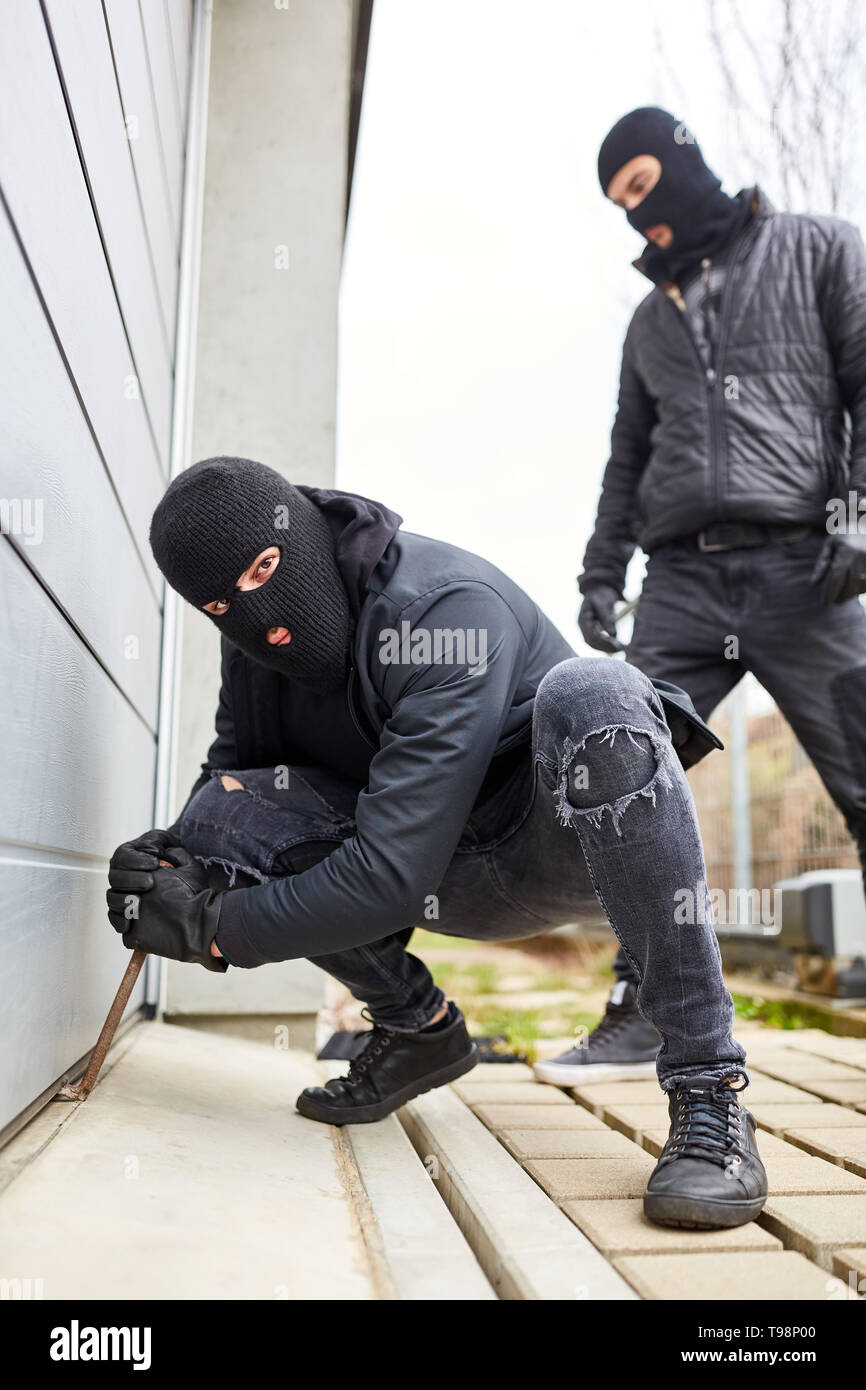 Two burglars at gate of garage with crowbar at burglary Stock Photo - Alamy