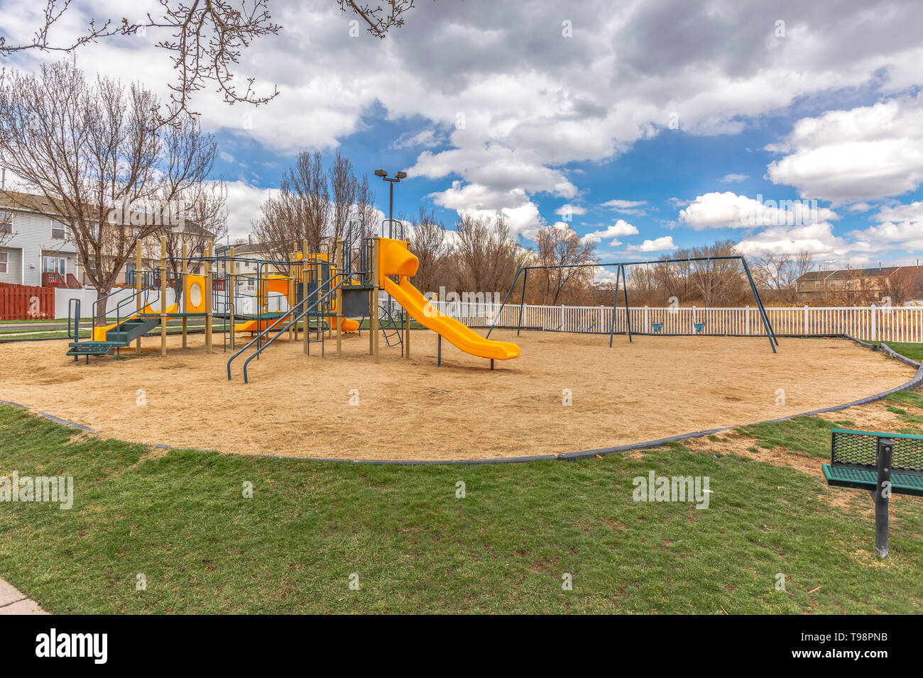 Bright yellow slides at a playground surrounded by a lawn with benches ...