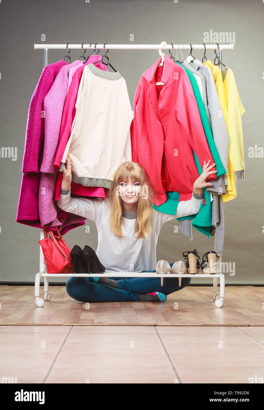 Pretty woman sitting under clothing from wardrobe. Young happy ...