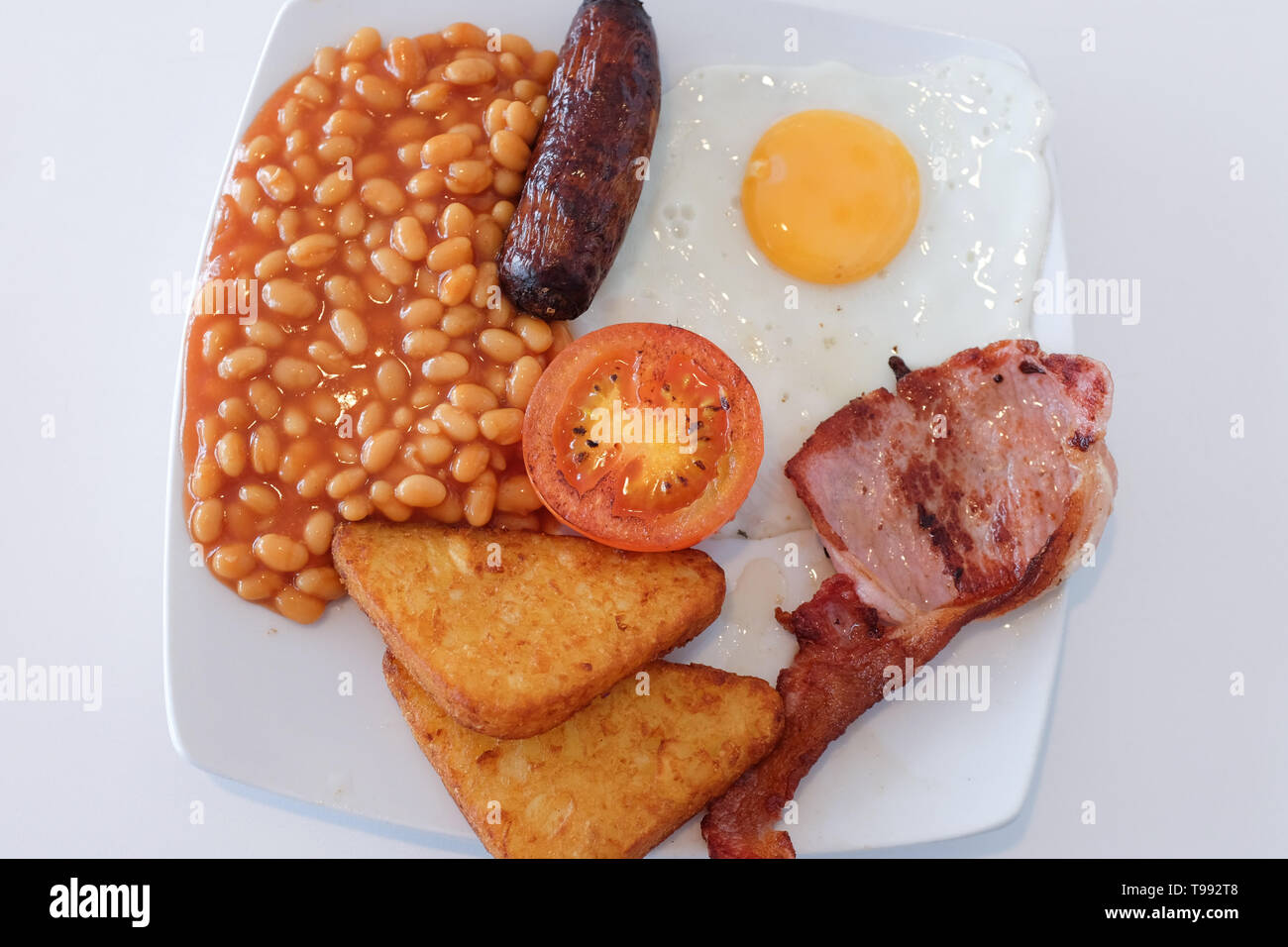 A full English breakfast comprising egg, beans, sausage, hash browns, bacon, and tomato Stock ...