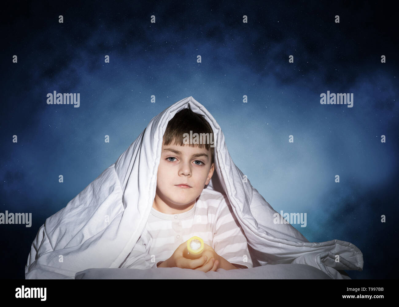 Serious child with flashlight hiding under blanket Stock Photo - Alamy