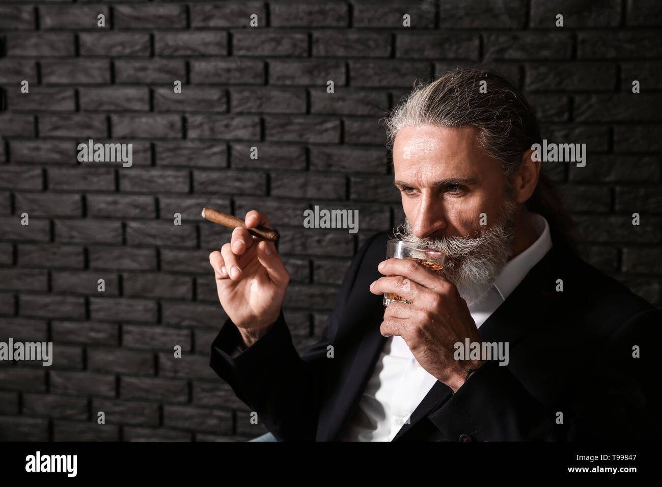 Senior man drinking whiskey and smoking cigar near dark brick wall Stock Photo - Alamy
