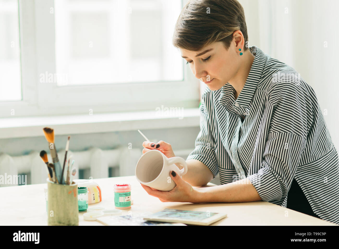the pottery woman holds in hands a mug to paint the ornament, handmade ...