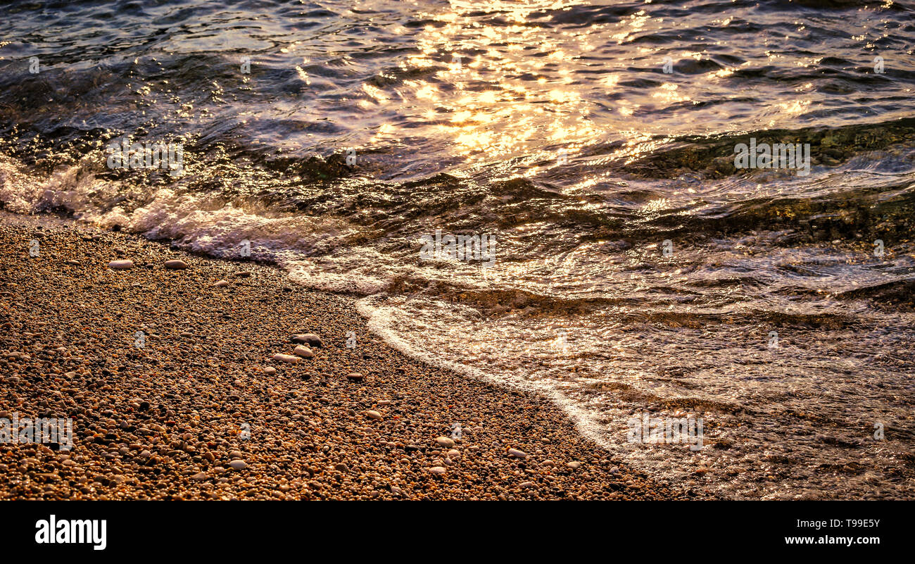Close-up view of pebble beach at sunset, sun reflects on the water ...