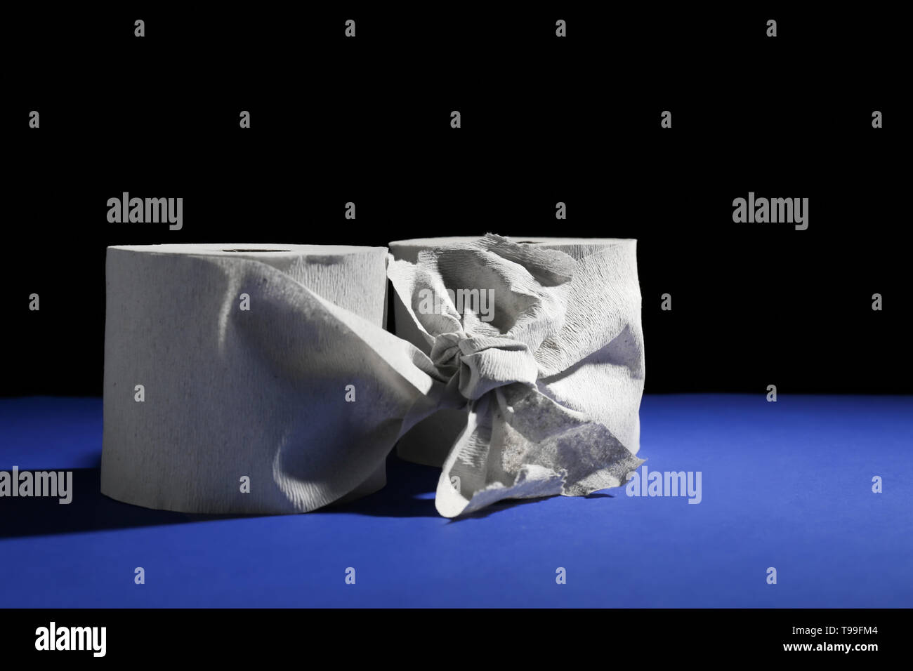 Tied rolls of soft toilet paper on color table against dark background ...