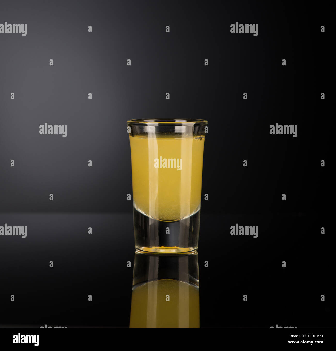 yellow alcoholic liquor in a shot glass isolated on dark background ...