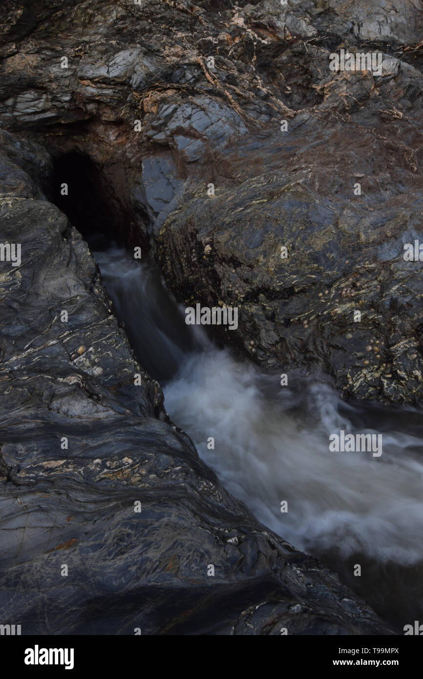 Water emerging from an adit mine at Maenporth Beach Cornwall Stock ...