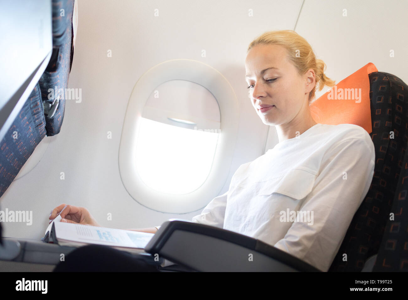 Woman reading in flight magazine on airplane. Female traveler reading ...