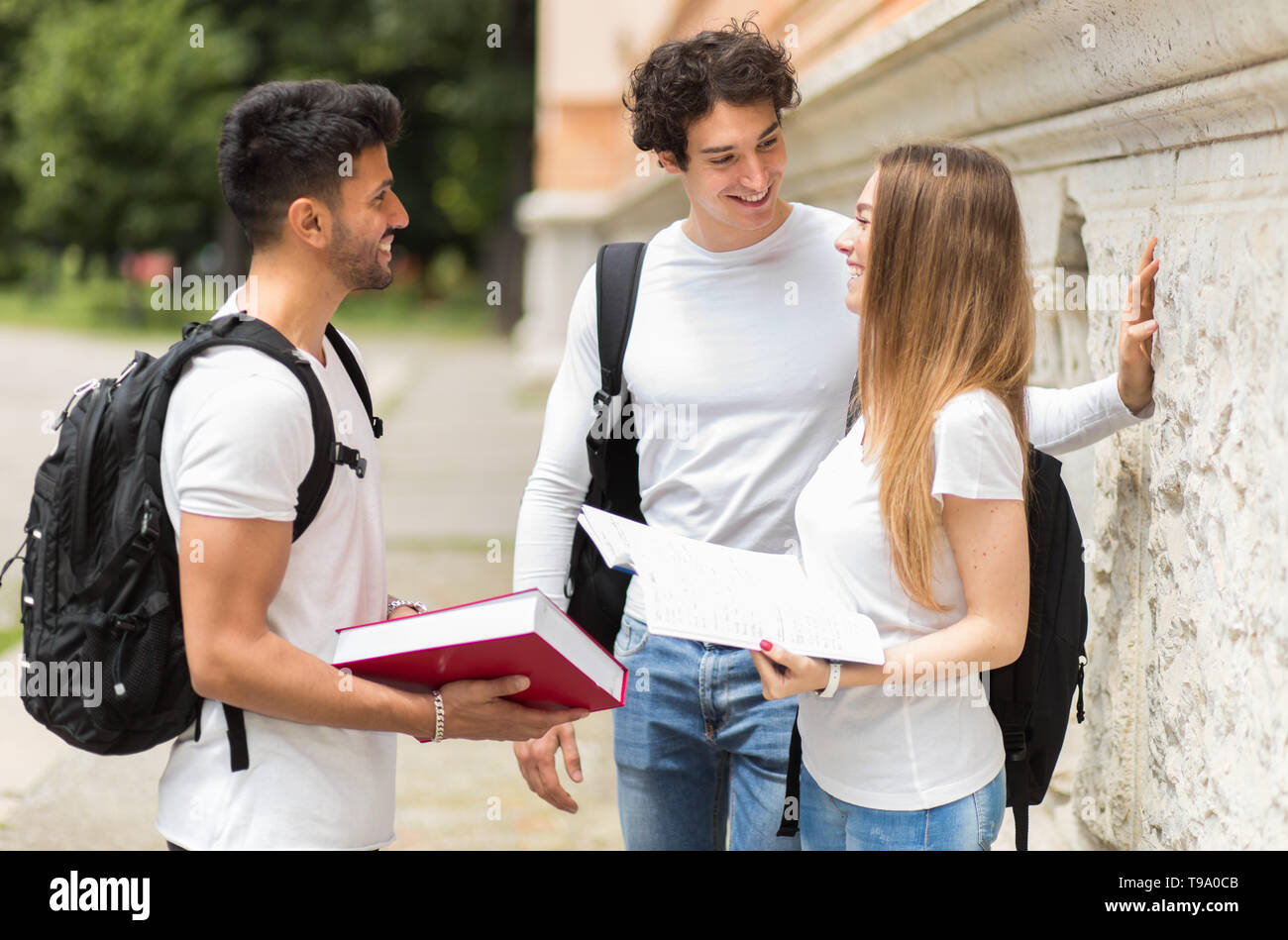 Three students talking to each other outdoor in a college courtyard ...