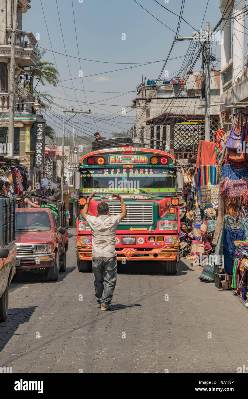 A man directing a colorful public bus through a narrow street, with ...
