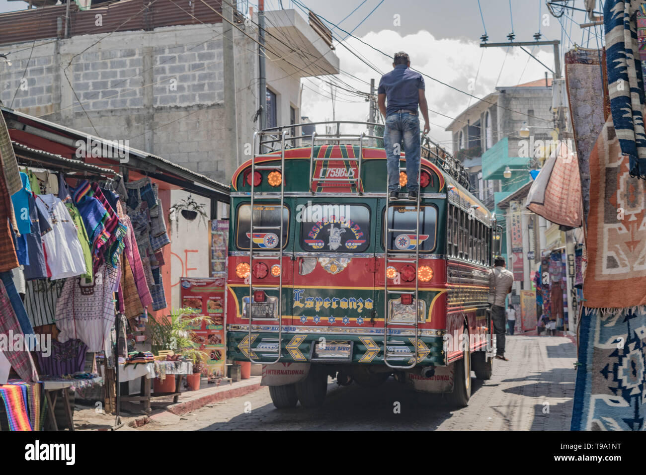 A man directing a colorful public bus through a narrow street, with ...