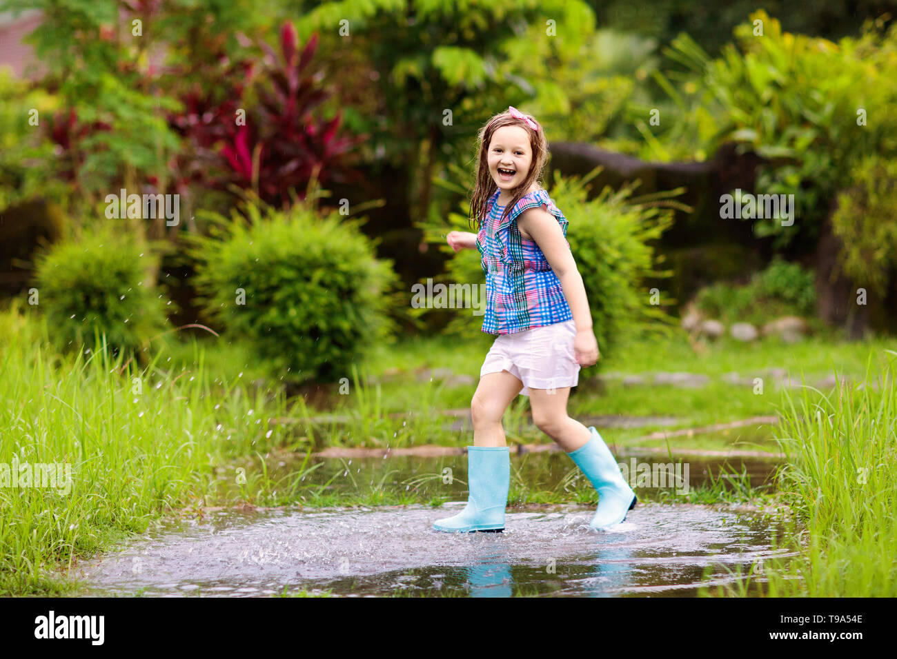 Kid playing out in the rain. Children with umbrella and rain boots play ...