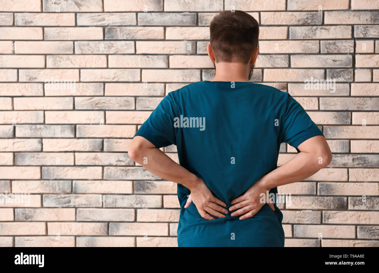 Man suffering from back pain against brick wall Stock Photo - Alamy