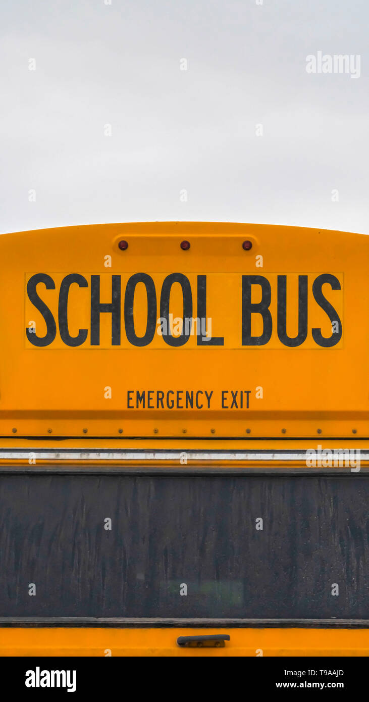 Vertical Close up of the back side of a yellow school bus against homes ...