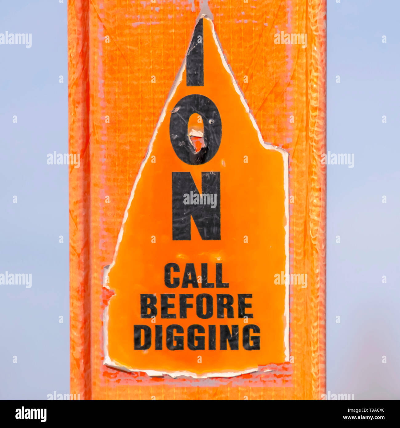 Square A torn Caution sign on a bright orange post against a blurry ...