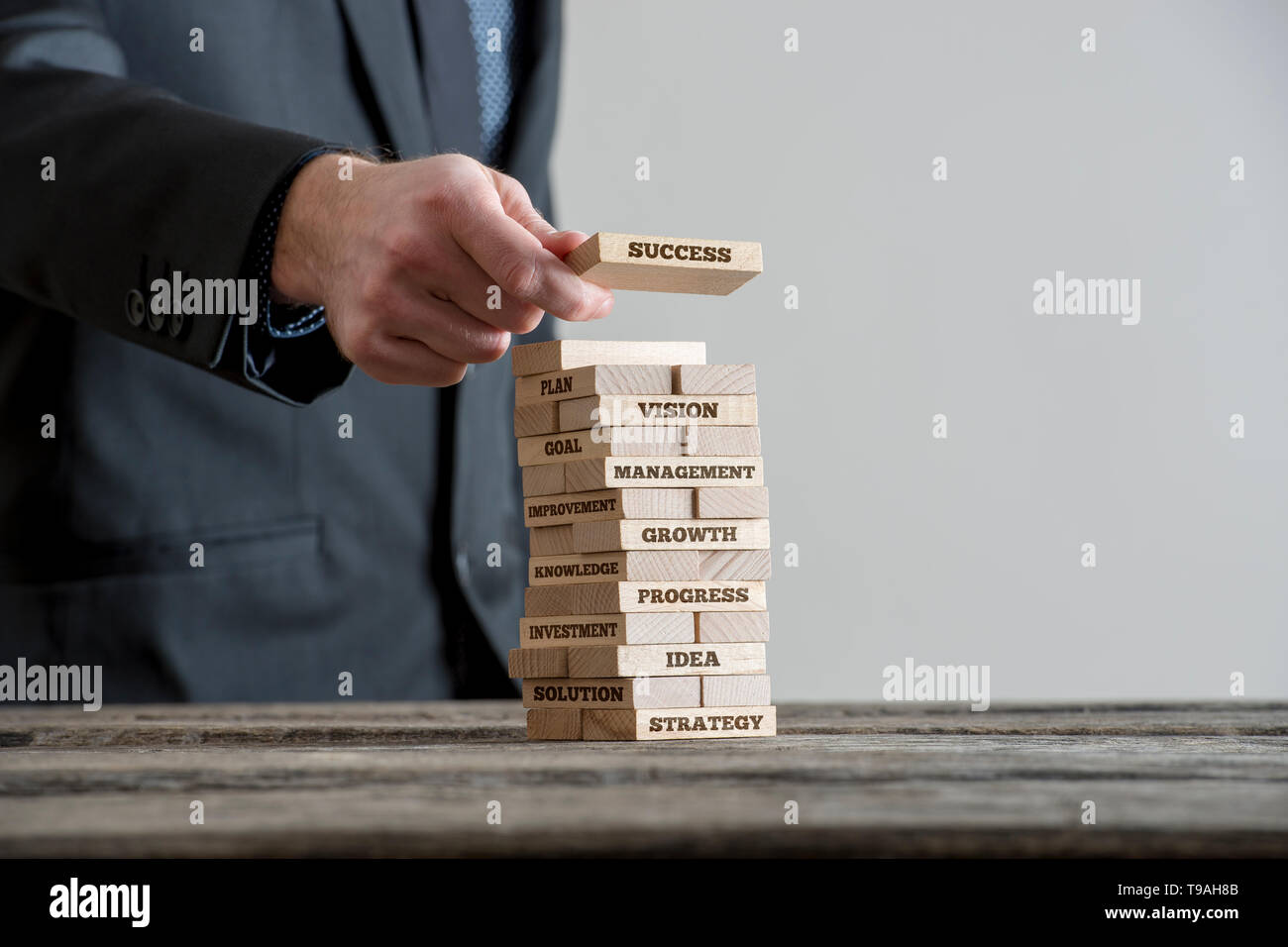 Businessman in black suite building tower of wooden domino bricks with ...