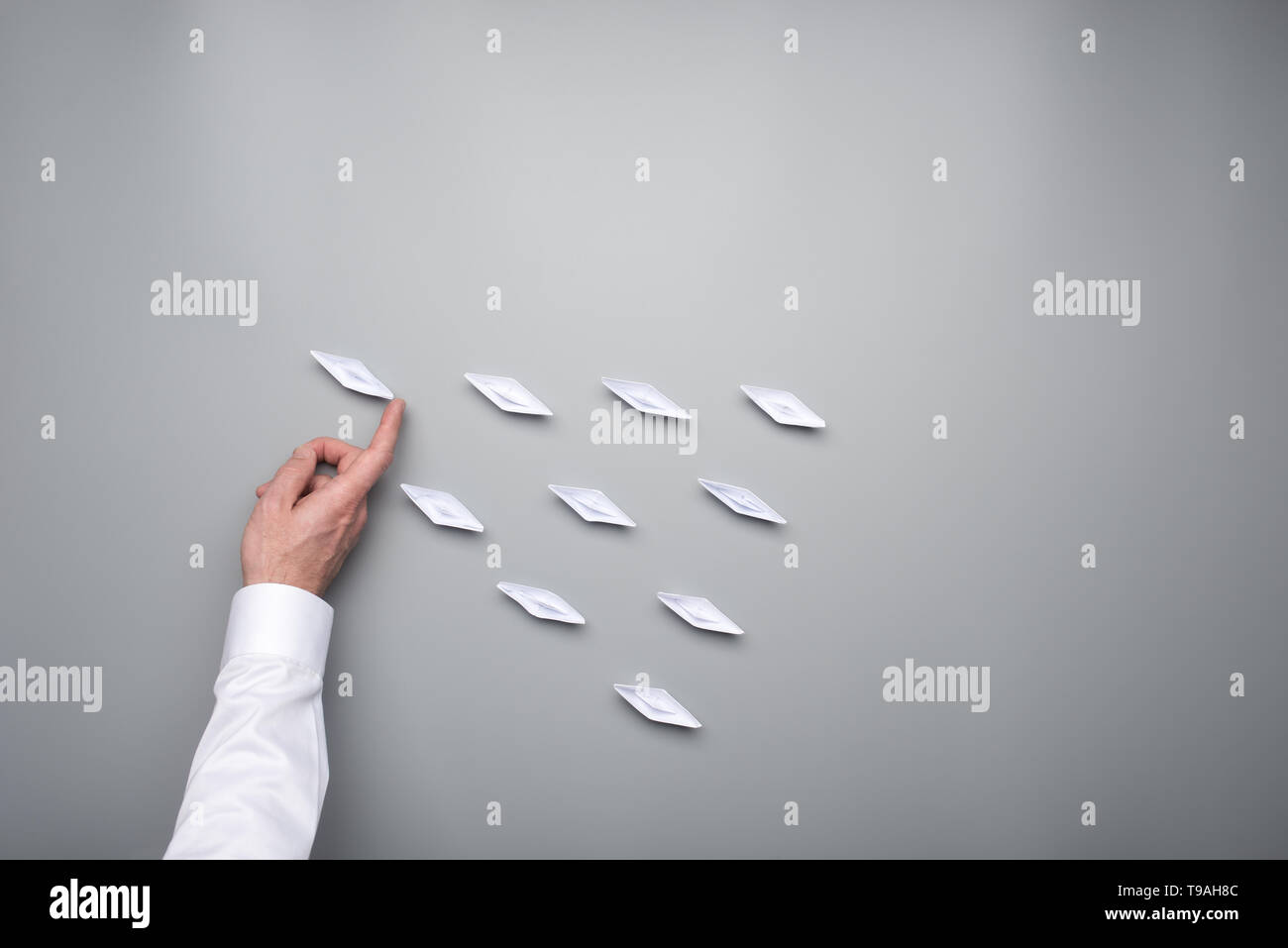Hand of a businessman pushing one of the origami paper made boats ...