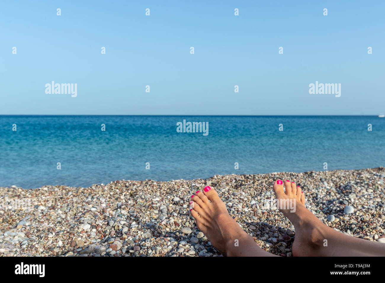 Female Feet With Pink Pedicure On A Beautiful Pebble Beach By Calm Blue
