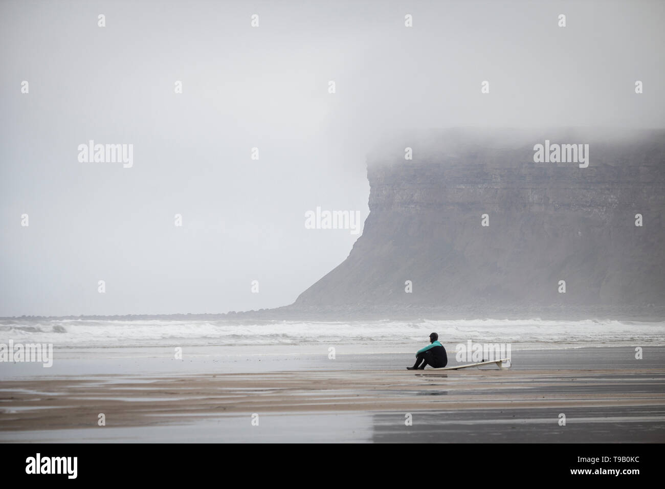 Surfer under mist shrouded cliffs at Saltburn by the sea, North ...