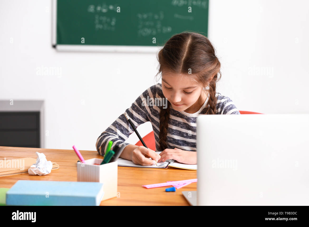 Cute girl doing homework in classroom Stock Photo - Alamy