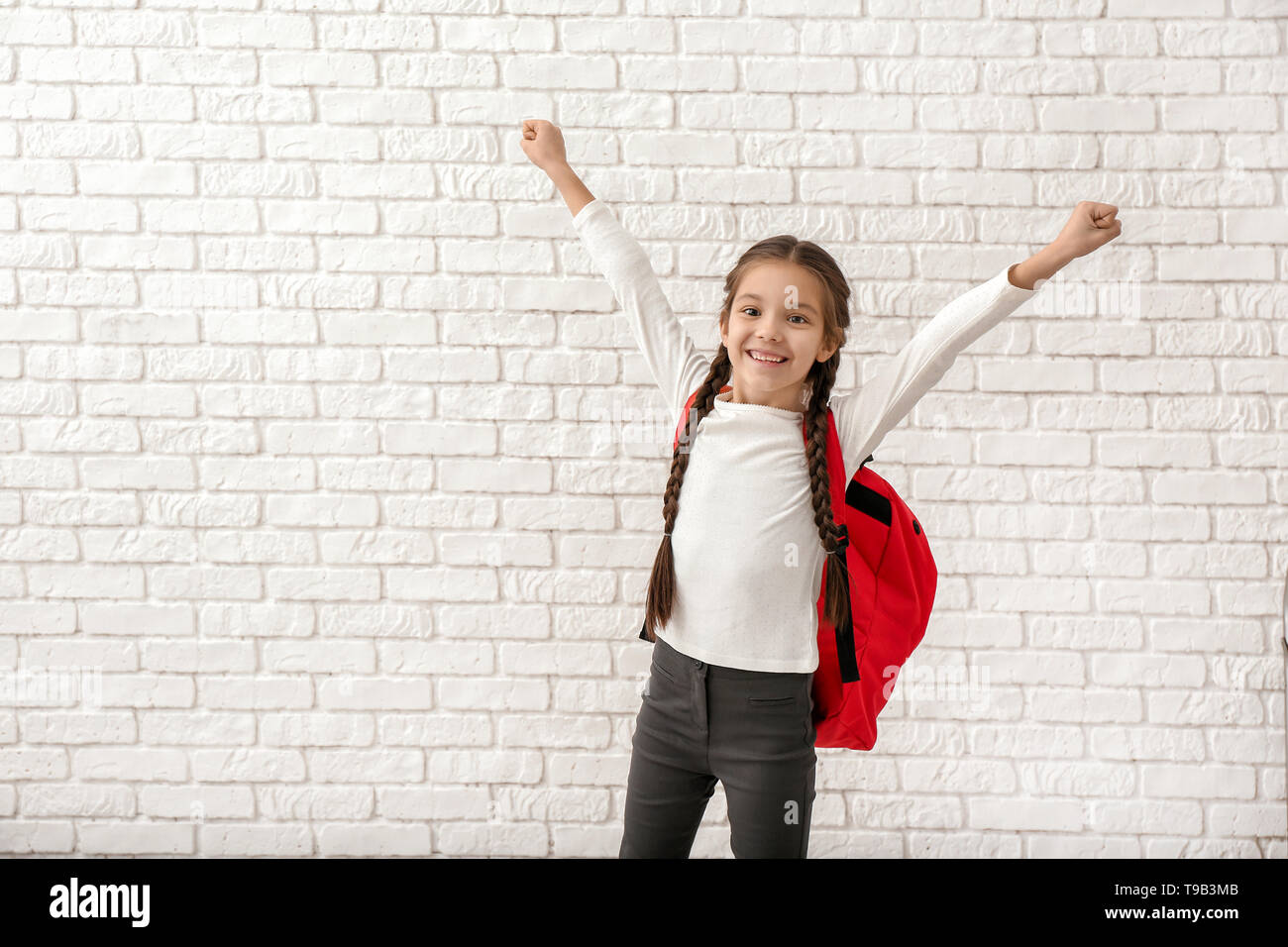 Happy girl with backpack on white brick background Stock Photo - Alamy