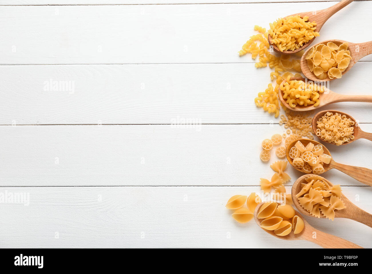 Spoons with different types of raw pasta on white wooden table Stock ...