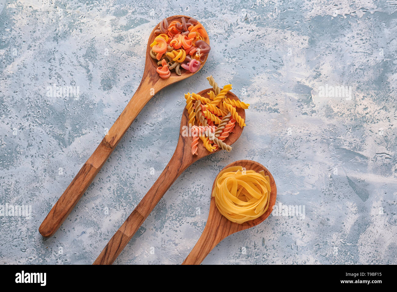 Spoons with different types of raw pasta on color table Stock Photo - Alamy