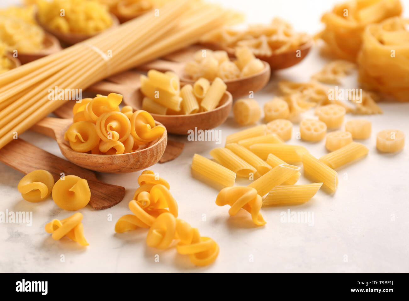 Spoons with different types of raw pasta on white table Stock Photo - Alamy