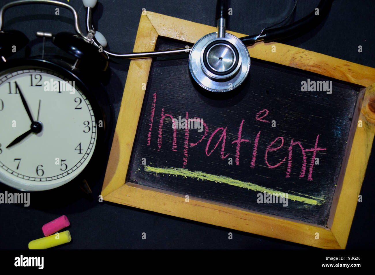 The words Inpatient handwriting on chalkboard on top view. Alarm clock ...