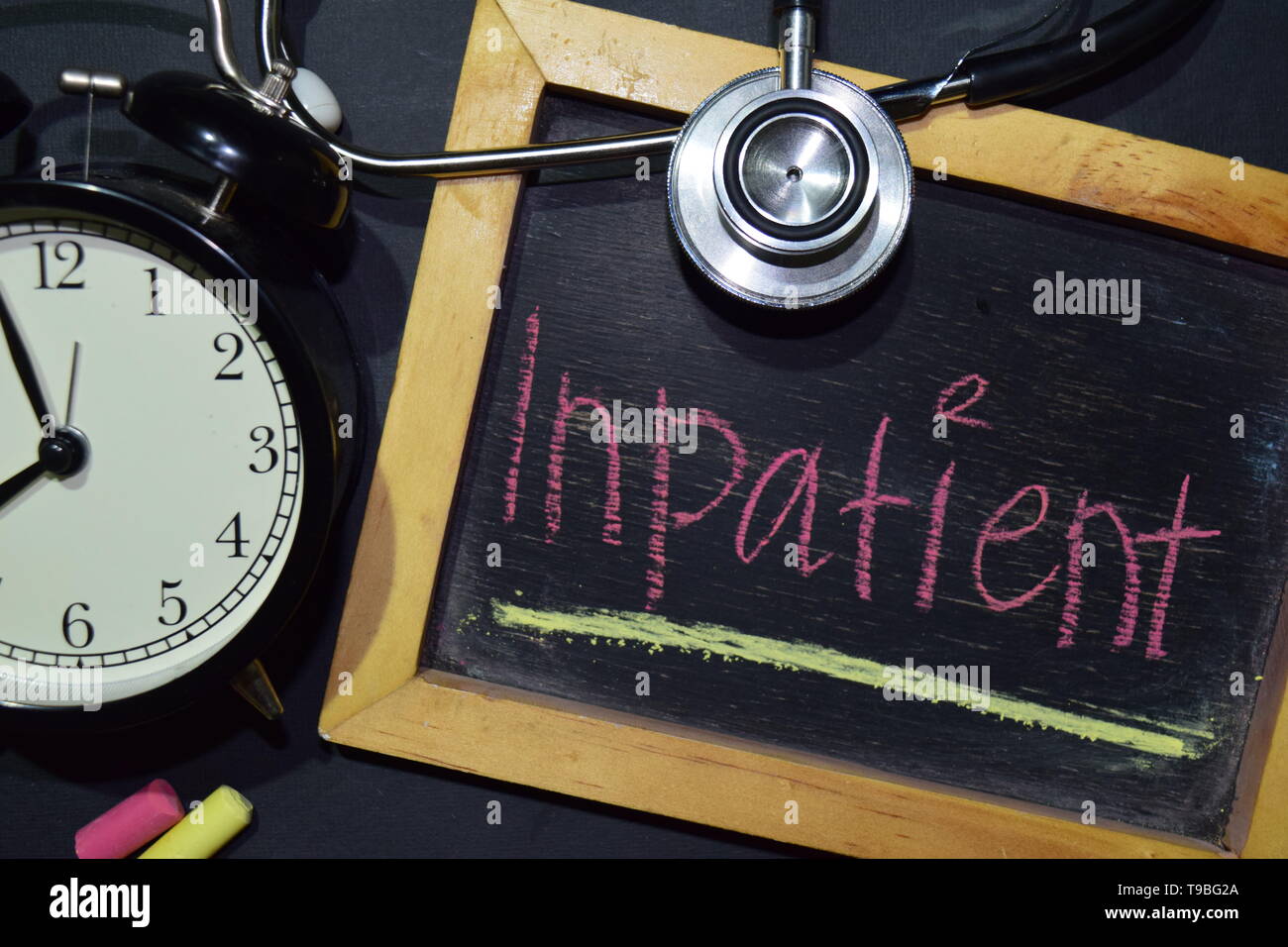 The words Inpatient handwriting on chalkboard on top view. Alarm clock ...