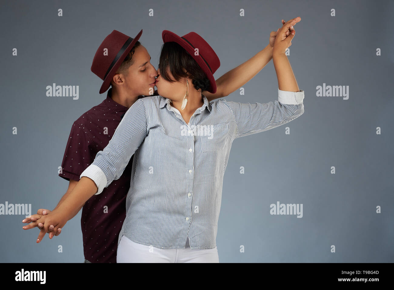 Kissing young couple in hats isolated on gray studio background Stock ...